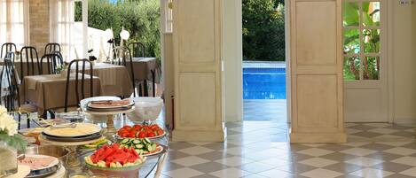Uma mesa de buffet com diversos alimentos e uma piscina visível ao fundo.