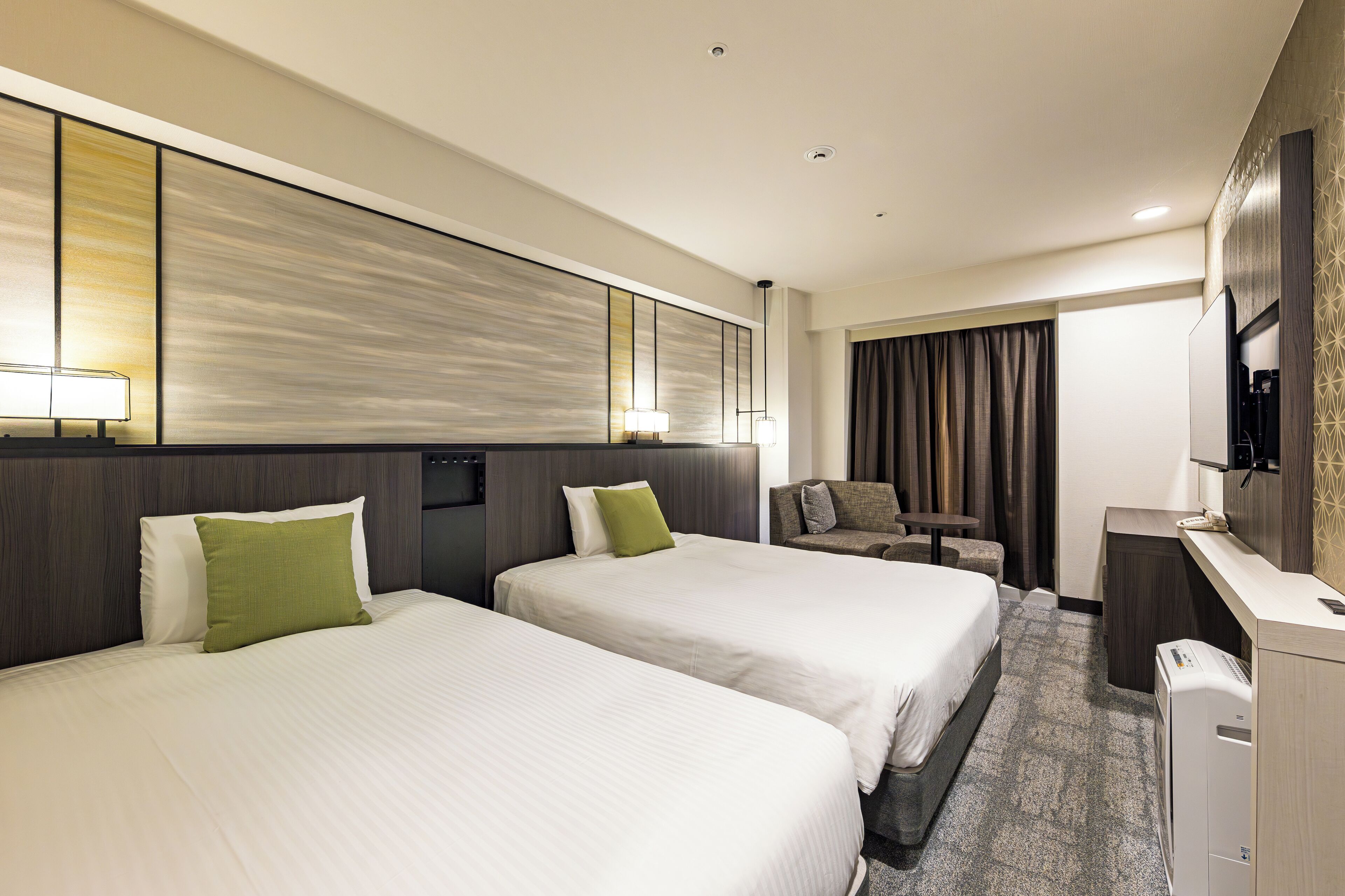 Quarto de hotel com duas camas, uma escrivaninha, uma cadeira e uma televisão.