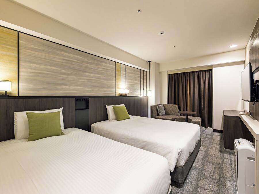 Quarto de hotel com duas camas, uma escrivaninha, uma cadeira e uma televisão.