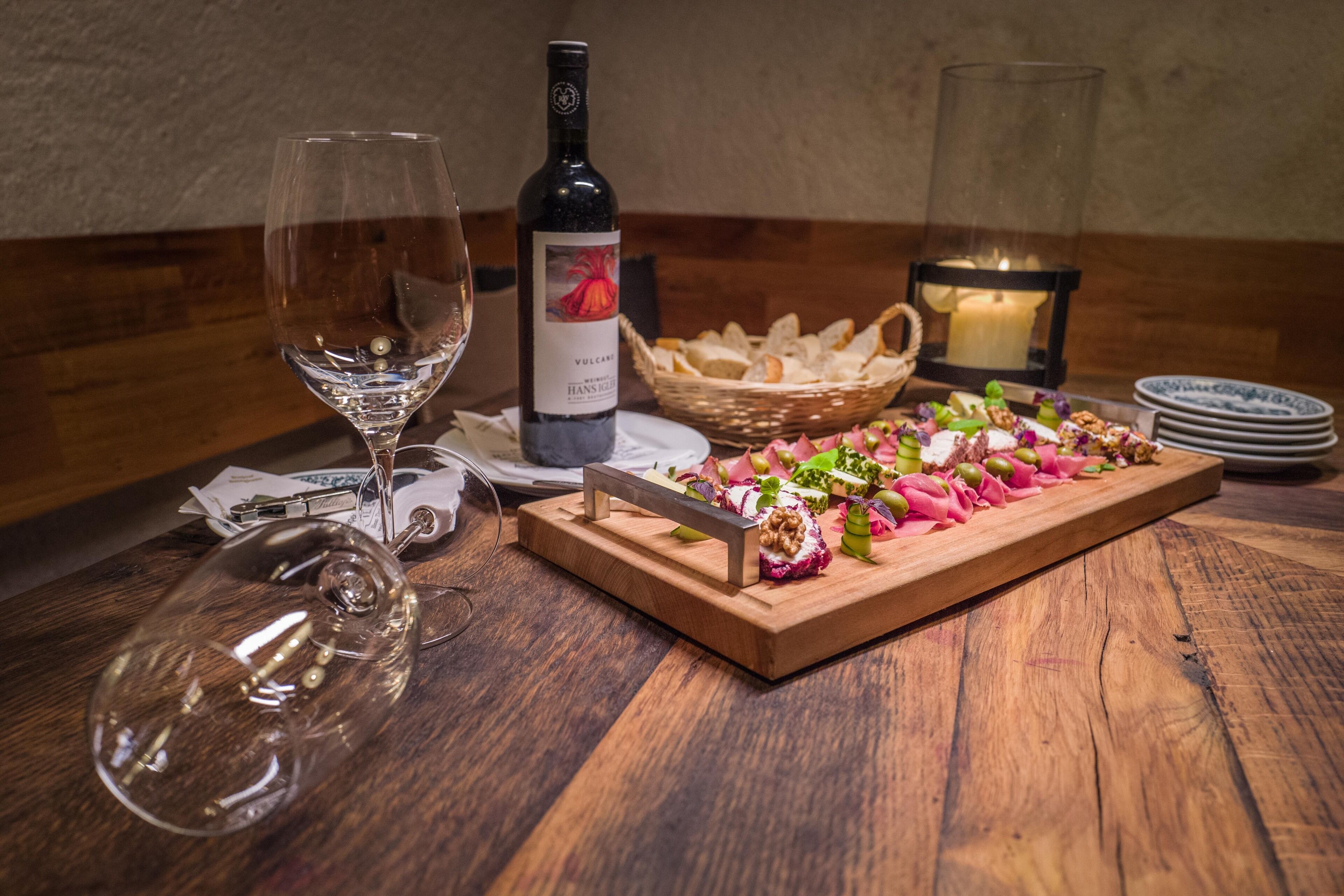 Uma mesa de madeira com uma garrafa de vinho, um copo, uma vela e uma tábua de madeira com comida.