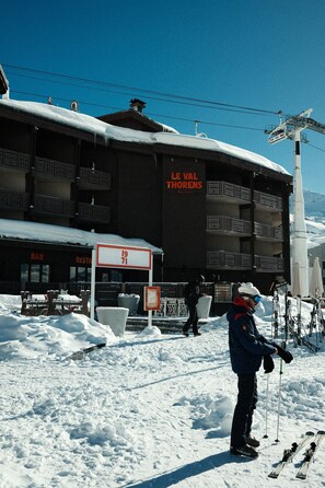 Uma estância de esqui com um edifício identificado como "LE VAL THORENS" e área externa com mesas e cadeiras.