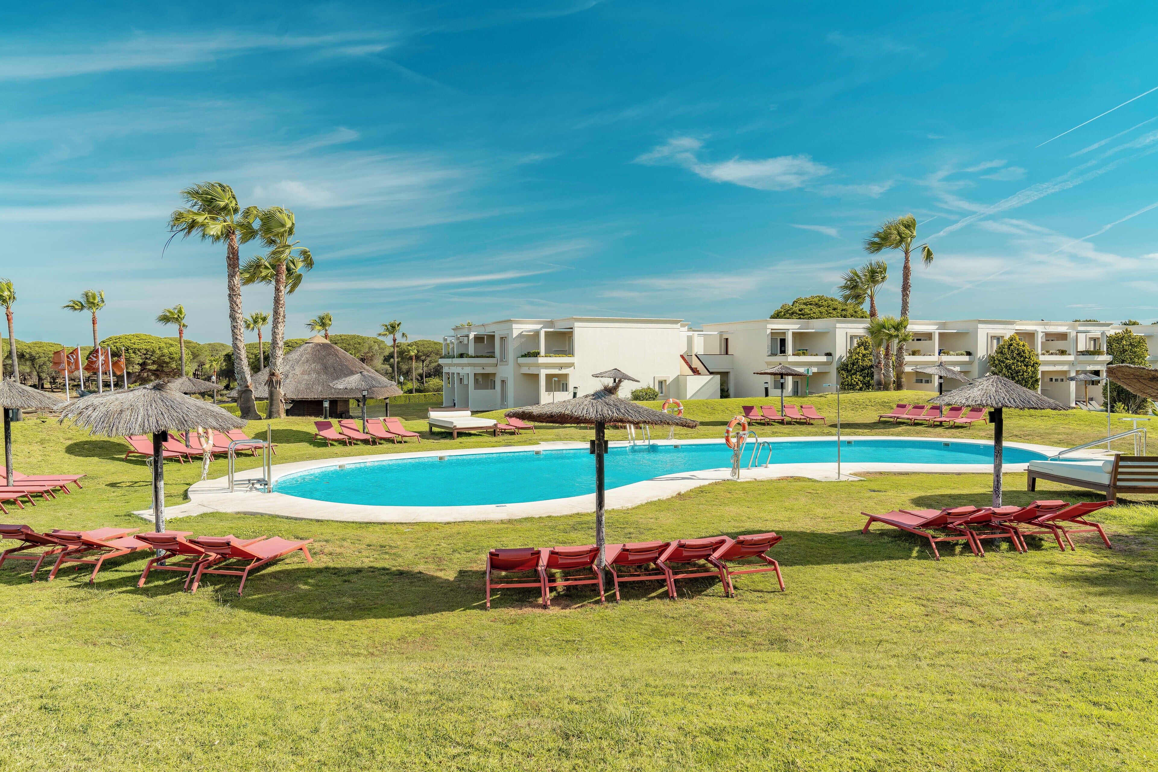 Um resort com piscina, espreguiçadeiras vermelhas e palmeiras.