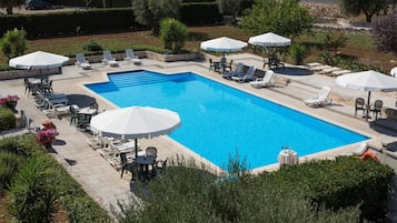 Piscina retangular com espreguiçadeiras e guarda-sóis, cercada por vegetação e um muro de pedra.