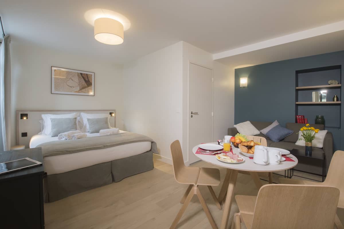 Quarto de hotel moderno com uma cama, uma mesa de jantar com café da manhã, um sofá e uma estante de livros.