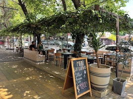 Café ao ar livre com mesas, cadeiras, cardápio em lousa e plantas em vasos.
