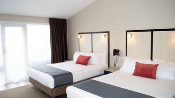 Quarto de hotel com duas camas, uma janela grande com cortinas e um telefone na parede.