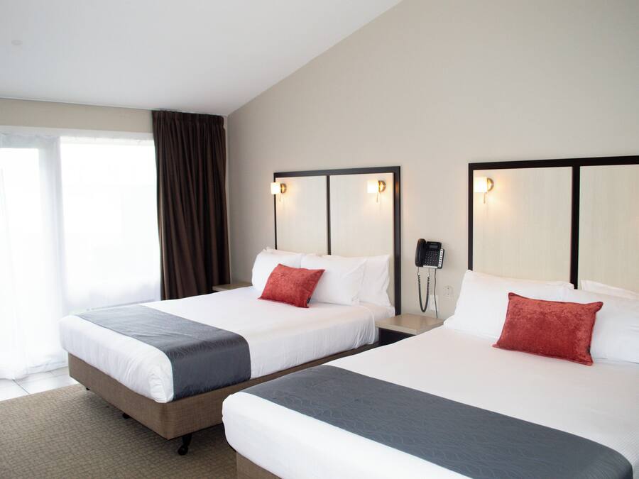 Quarto de hotel com duas camas, uma janela grande com cortinas e um telefone na parede.