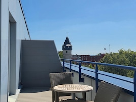 Varanda com vista para uma torre, mobiliário de vime e guarda-corpo.