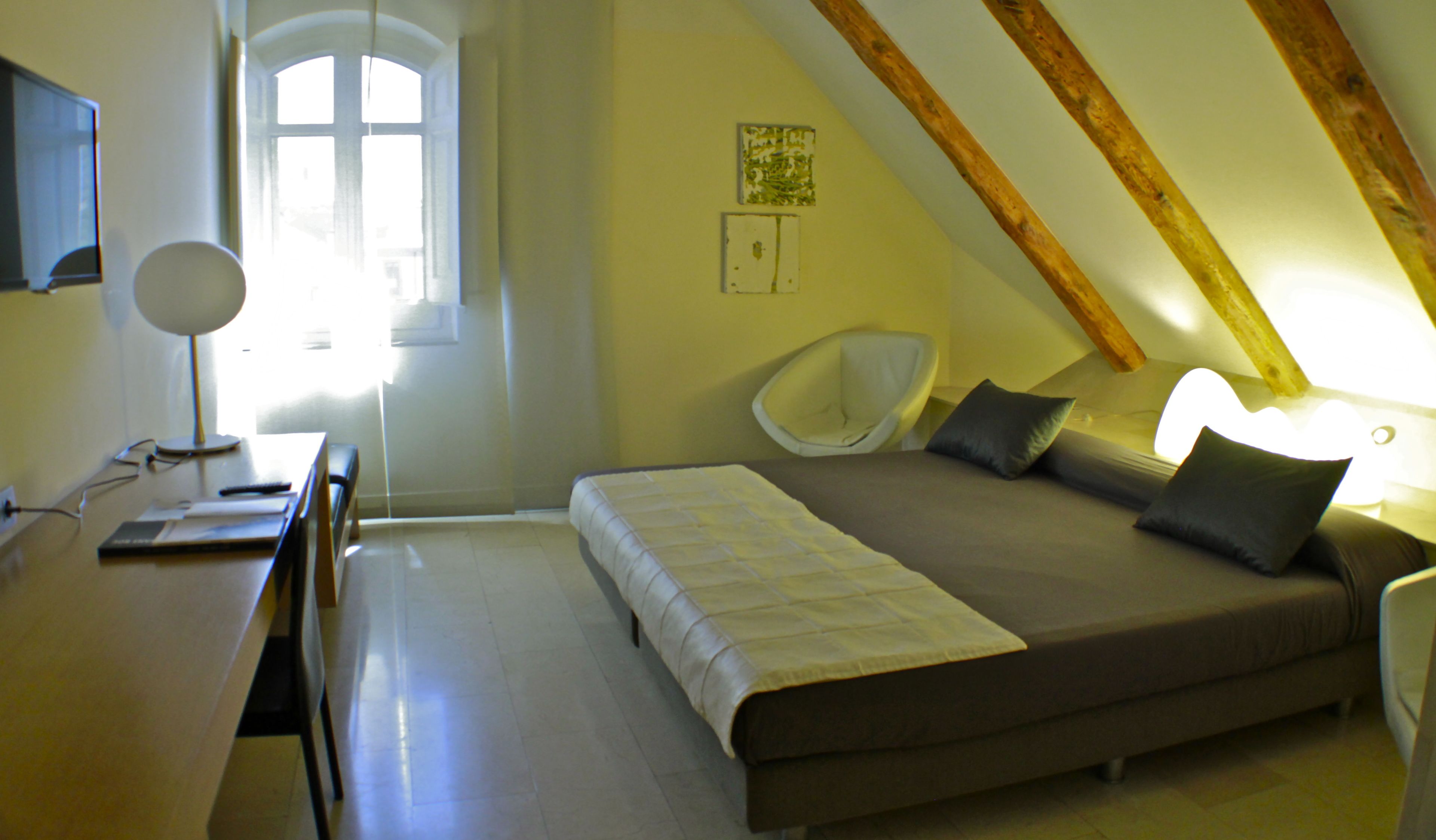 Um quarto com cama, escrivaninha, cadeira e janela.
