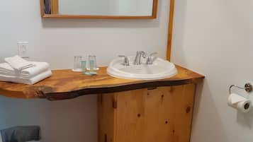 Um banheiro com toucador de madeira, espelho, pia e vaso sanitário.