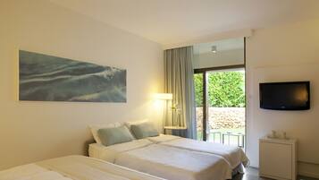 Quarto de hotel com duas camas, televisão, um quadro e varanda com vista para o verde.