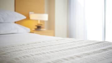 Quarto de hotel com uma cama, almofadas, mesa de cabeceira com abajur e uma janela.