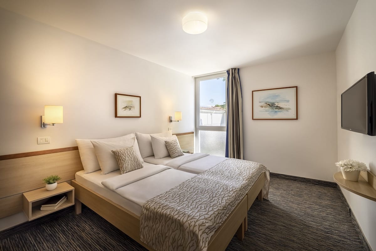 Quarto de hotel com uma cama grande, mesas de cabeceira, televisão de tela plana e obras de arte nas paredes.