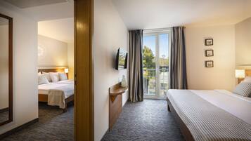 Quarto de hotel com cama, televisão, uma mesinha e vista para o exterior através de uma porta de vidro.