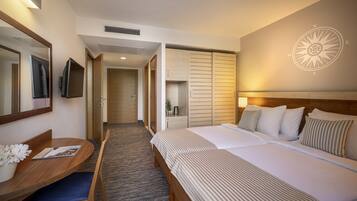 Quarto de hotel com cama, escrivaninha com cadeira, televisão e bússola fixada na parede.