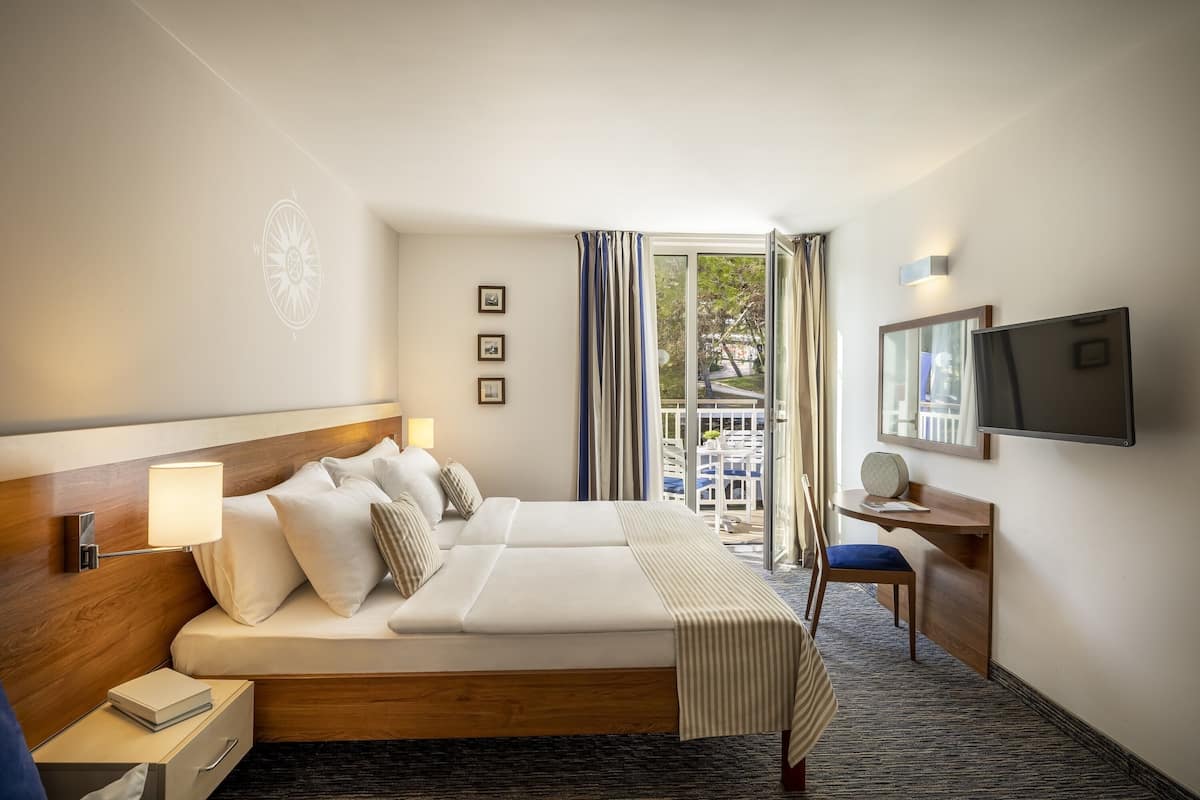 Quarto de hotel com cama grande, escrivaninha, televisão e vista para o exterior.