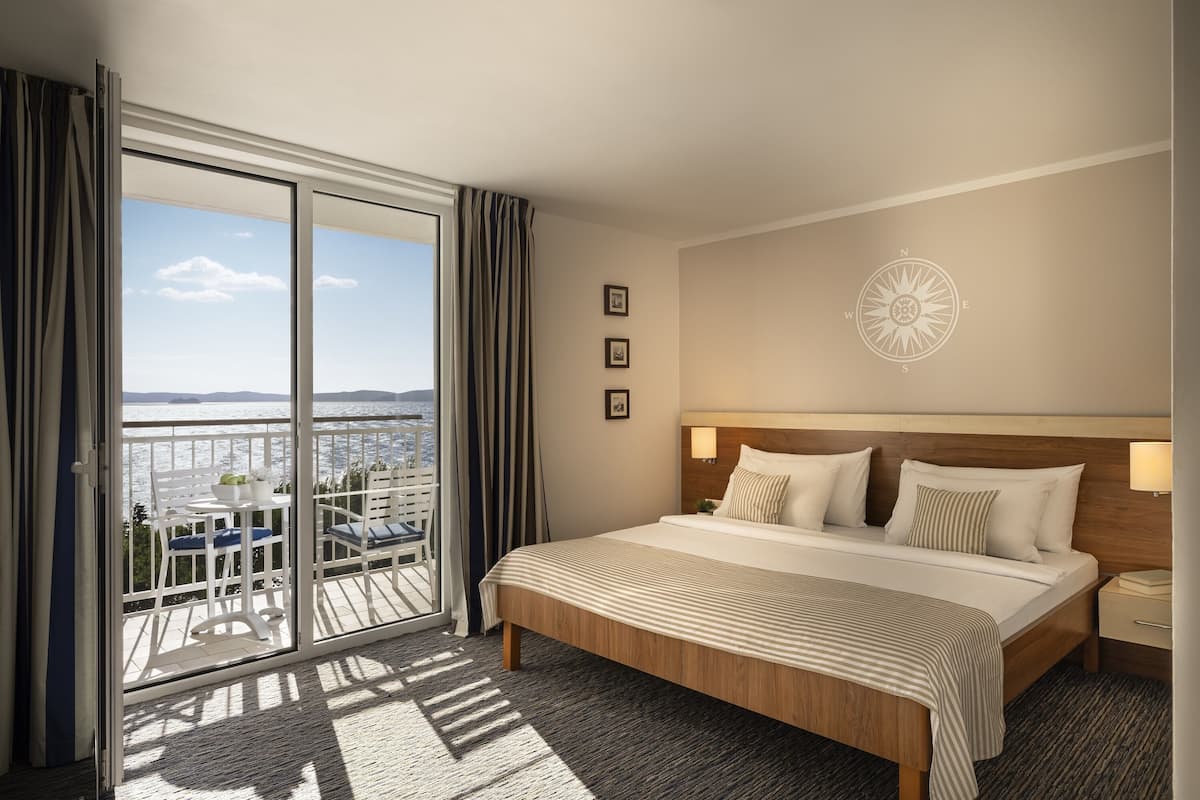 Quarto de hotel com uma cama grande, vista da cidade através de uma porta deslizante, cabeceira de madeira e decoração de parede com uma bússola.