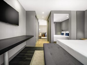 Quarto de hotel moderno com televisão de ecrã plano, sofá, cama e uma pequena mesa.