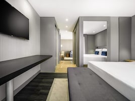 Quarto de hotel moderno com televisão de ecrã plano, sofá, cama e uma pequena mesa.