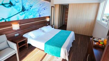 Quarto de hotel com uma cama, mesa de cabeceira, uma cadeira, uma janela grande e uma bandeja com itens de café da manhã.
