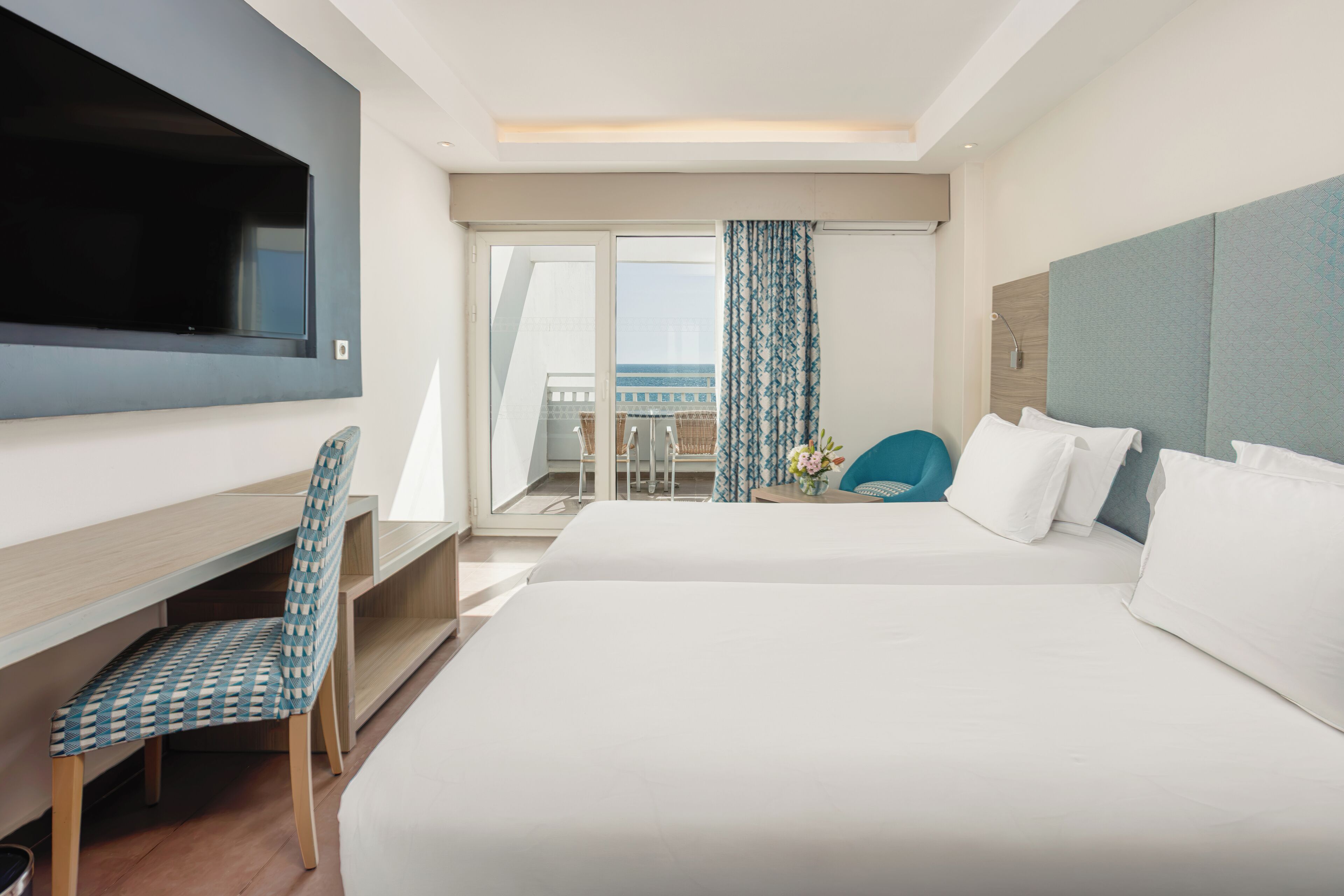 Quarto de hotel com cama, escrivaninha, cadeira, televisão e varanda com vista.