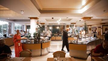 Ampla sala de jantar de hotel, com diversas opções de assentos e um buffet central.