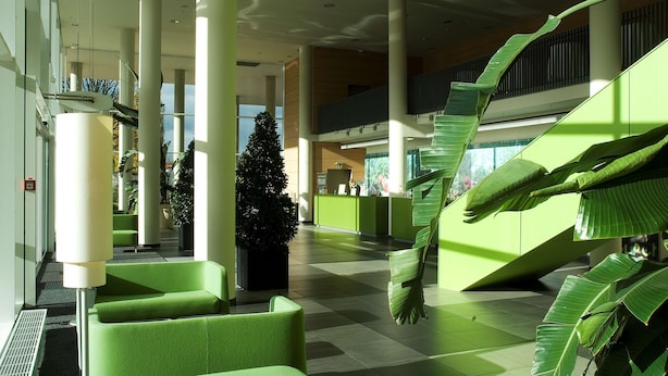 Um lobby moderno com assentos verdes, uma escada e um balcão de recepção.