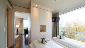 Quarto de hotel com uma cama grande, uma escrivaninha com cadeira, televisão e vista para árvores de outono.