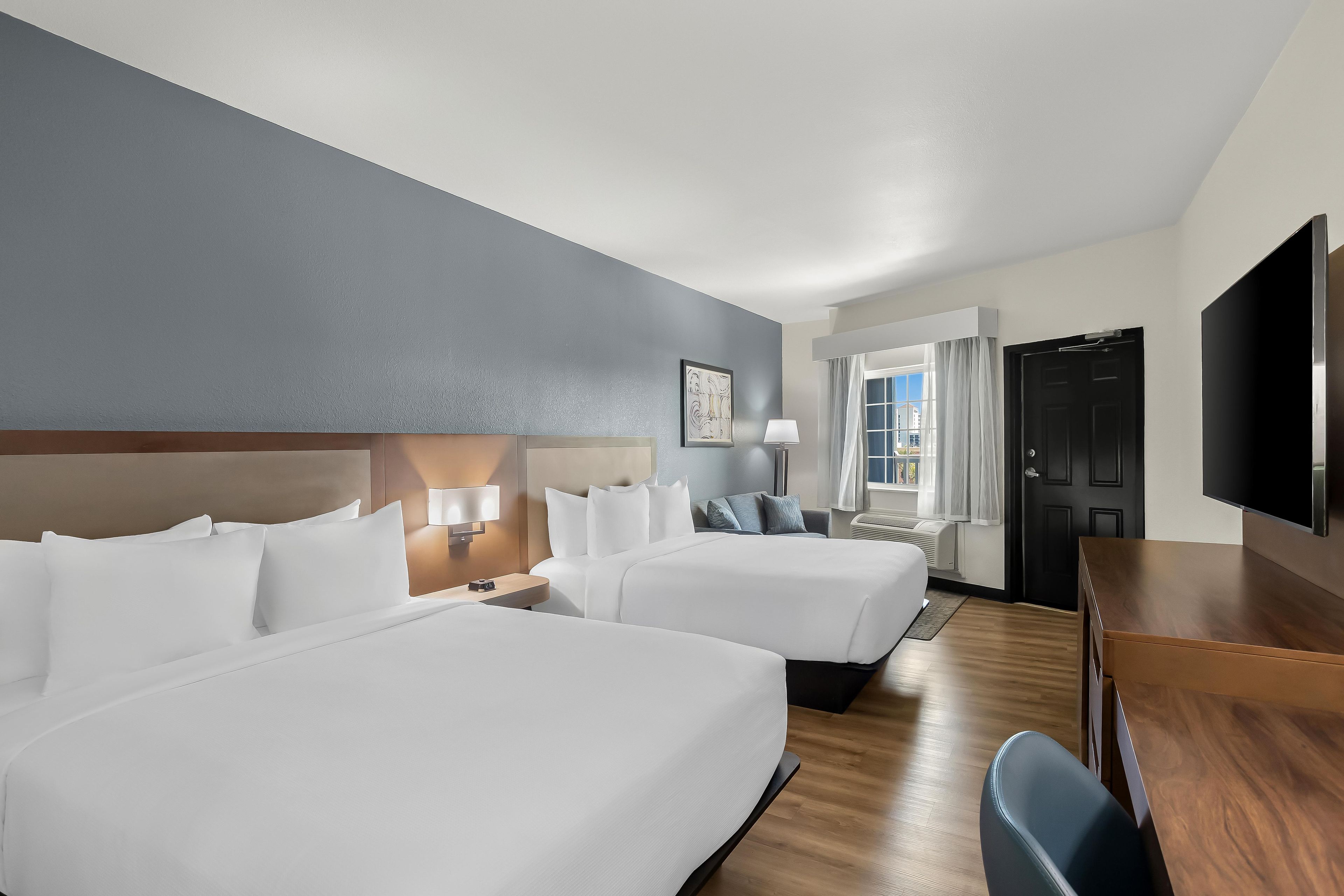 Quarto de hotel com duas camas, uma escrivaninha, televisão e janela com cortinas.