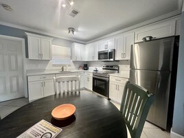 Cozinha moderna com armários brancos, eletrodomésticos de aço inoxidável e bancada escura.