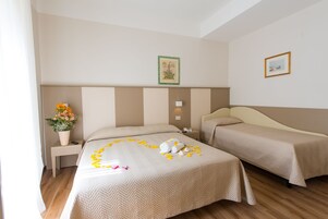Quarto de hotel com duas camas, uma mesinha de cabeceira com um vaso de flores e um quadro pendurado na parede.