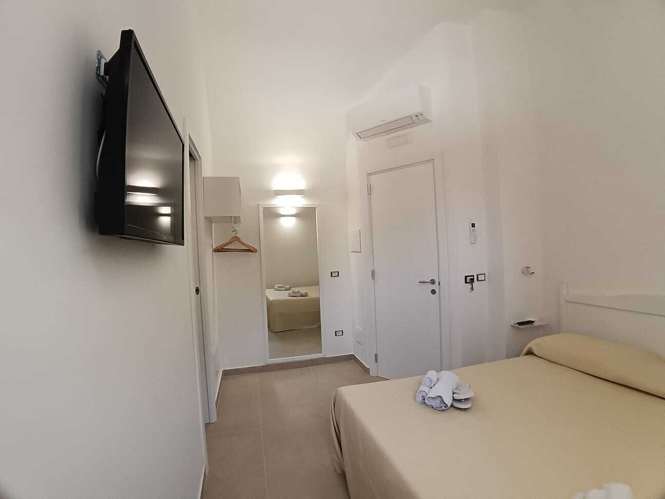 Quarto de hotel com cama, televisão fixada na parede, porta e espelho.