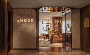 Um saguão de hotel com um letreiro chamativo 'AMBER', área de bar com garrafas e um conjunto de assentos.