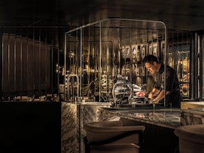 Uma área de bar com bancada de mármore, uma máquina de café e uma pessoa trabalhando atrás do balcão.