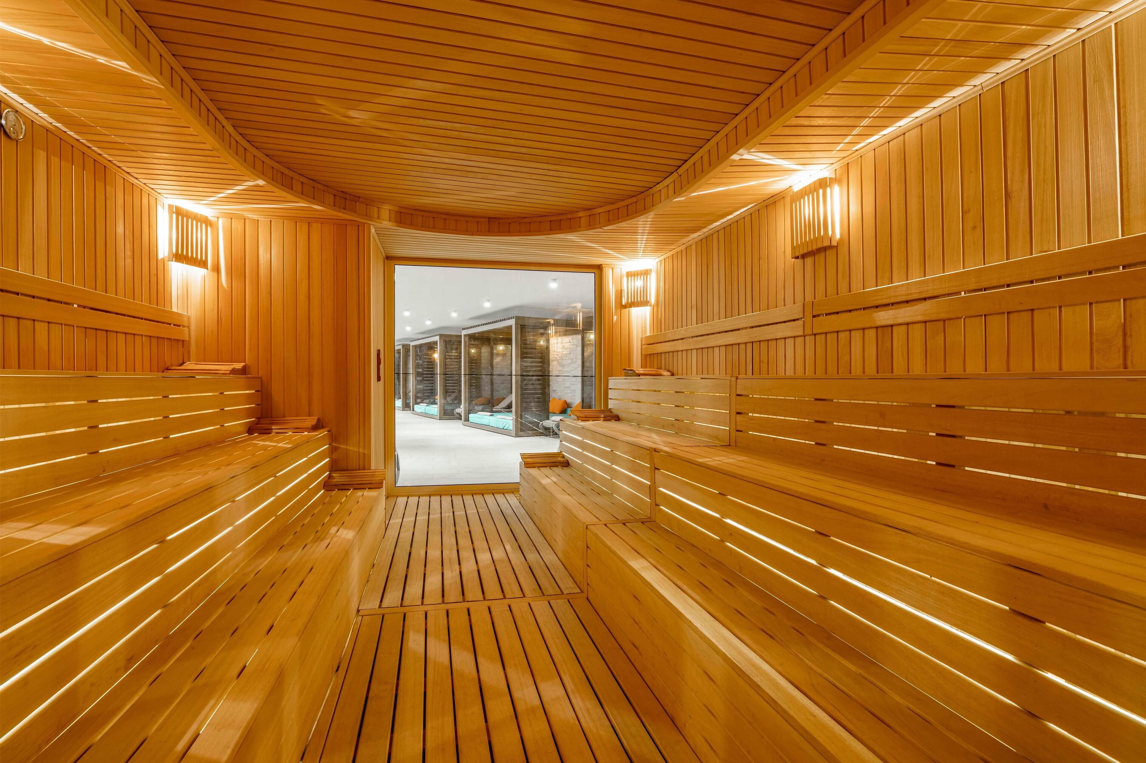 Uma sauna com bancos e paredes de madeira, entrada visível e porta de vidro que dá para o exterior.