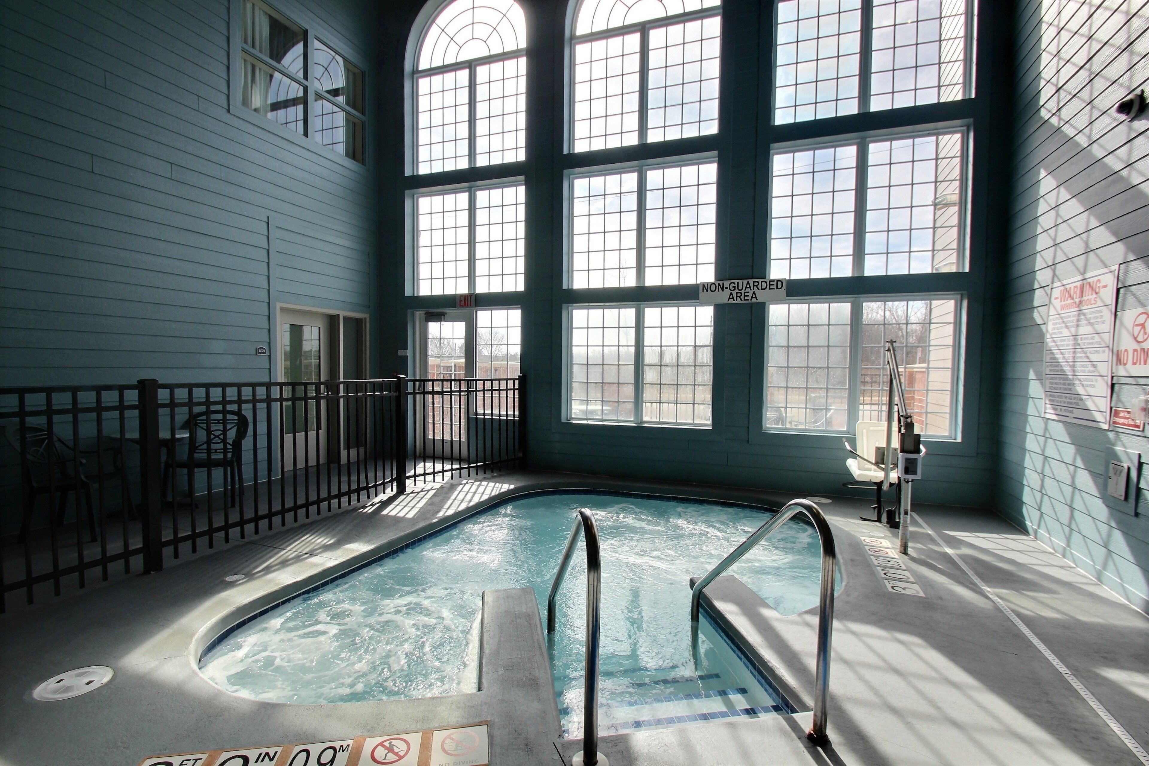 Piscina interna com área não vigilância, banheira de hidromassagem e vista para o exterior através de grandes janelas.