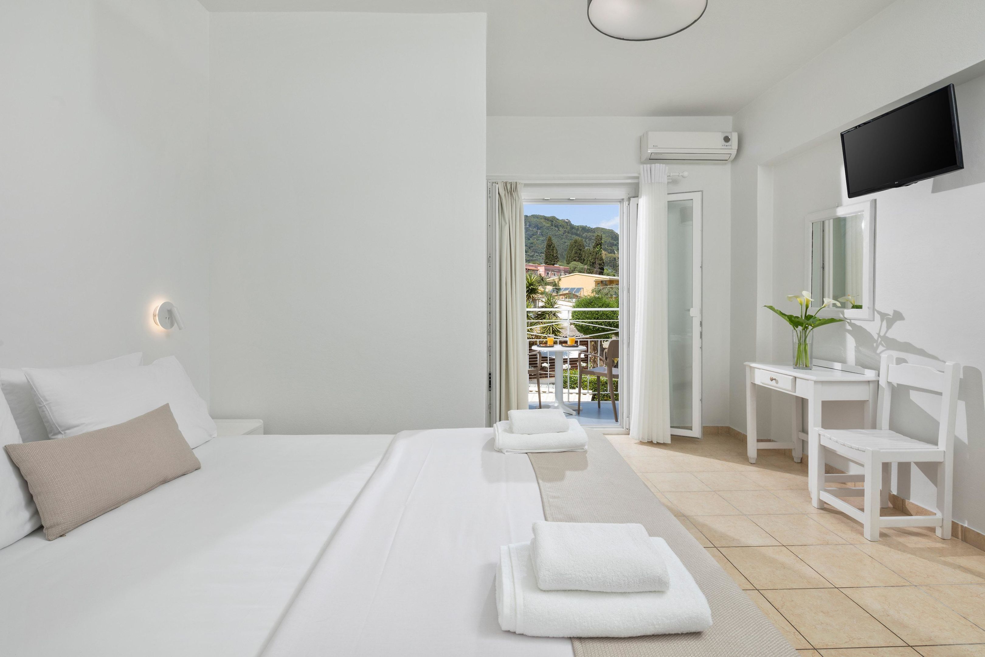 Quarto de hotel com cama, escrivaninha, cadeira, televisão e vista para o exterior.