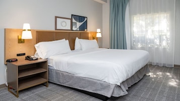 Quarto de hotel com uma cama grande, duas luminárias de cabeceira, mesa de cabeceira com telefone e uma janela com cortinas.