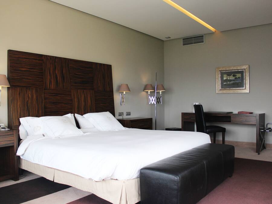 Quarto de hotel com uma cama grande, uma escrivaninha, uma cadeira e duas luminárias.