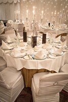 Uma sala de banquetes com mesas redondas preparadas para um evento formal, cada uma com toalhas brancas, talheres e copos.
