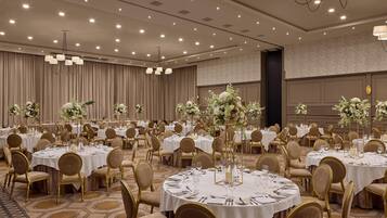 Uma sala de banquetes com mesas redondas, cadeiras douradas e arranjos florais.