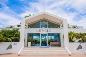 Um edifício moderno com fachada de vidro e a inscrição 'LE VELE' acima da entrada.