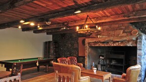 Um quarto acolhedor com mesa de bilhar, poltronas de couro, lareira e teto de madeira.