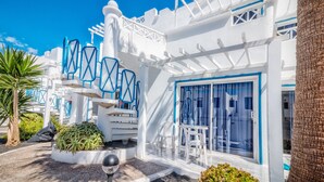 Um edifício branco com detalhes em azul, uma escadaria e um pátio com cadeiras e uma mesa.
