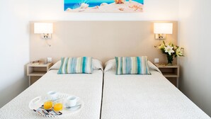 Quarto de hotel com duas camas, bandeja de café da manhã e uma pintura com tema praiano.
