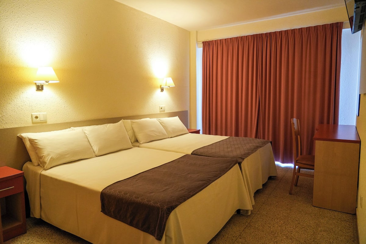 Quarto de hotel com uma cama de casal, uma escrivaninha e duas luminárias.