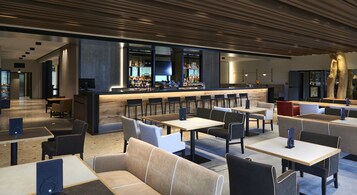 Uma área de bar moderna com diversas opções de assento, incluindo banquetas e mesas, e um balcão de bar com uma variedade de garrafas.