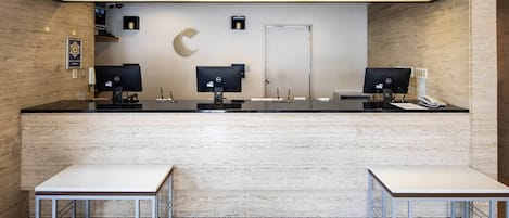 Um balcão de recepção com três monitores de computador, uma porta e uma decoração em formato de crescente lunar na parede.