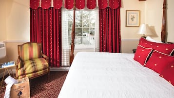 Quarto de hotel com uma cama grande, cortinas vermelhas, uma poltrona listrada e vista para o exterior.