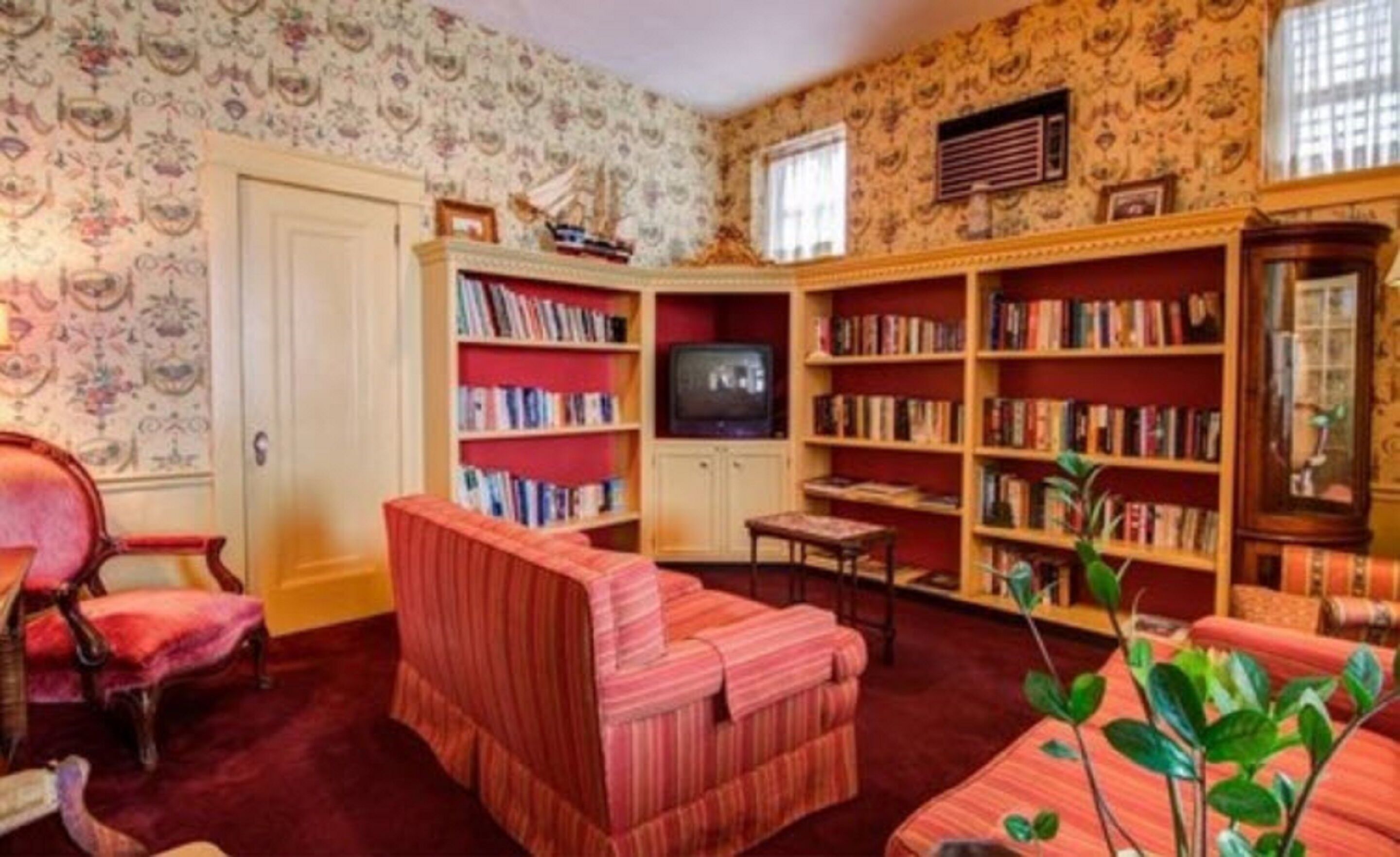 Uma sala de estar aconchegante com um sofá listrado, uma televisão e estantes repletas de livros.